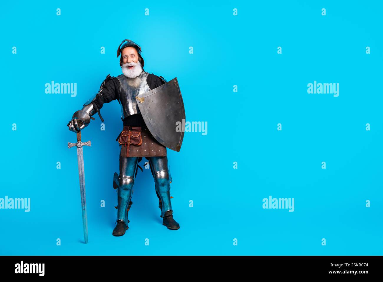 Elderly man in medieval knight costume posing against blue background ...
