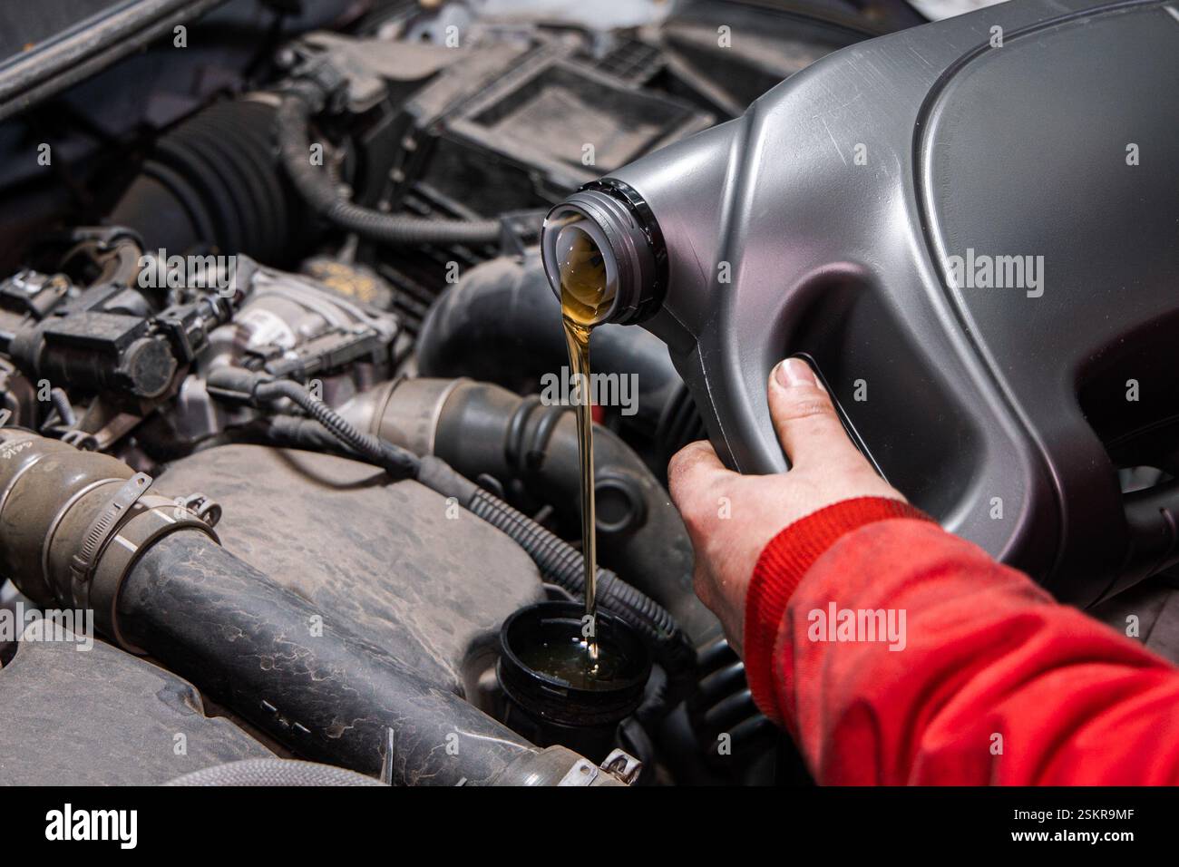 Close-up of a mechanic's hand pouring fresh engine oil from a large ...
