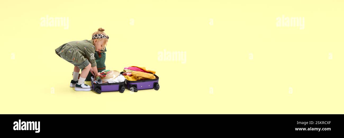 Pretty little girl, child in casual clothes carefully packing suitcase ...
