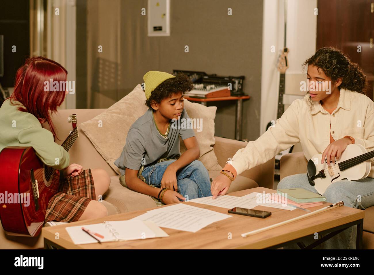 Band of three biracial teens sitting on sofa and chair at studio while ...