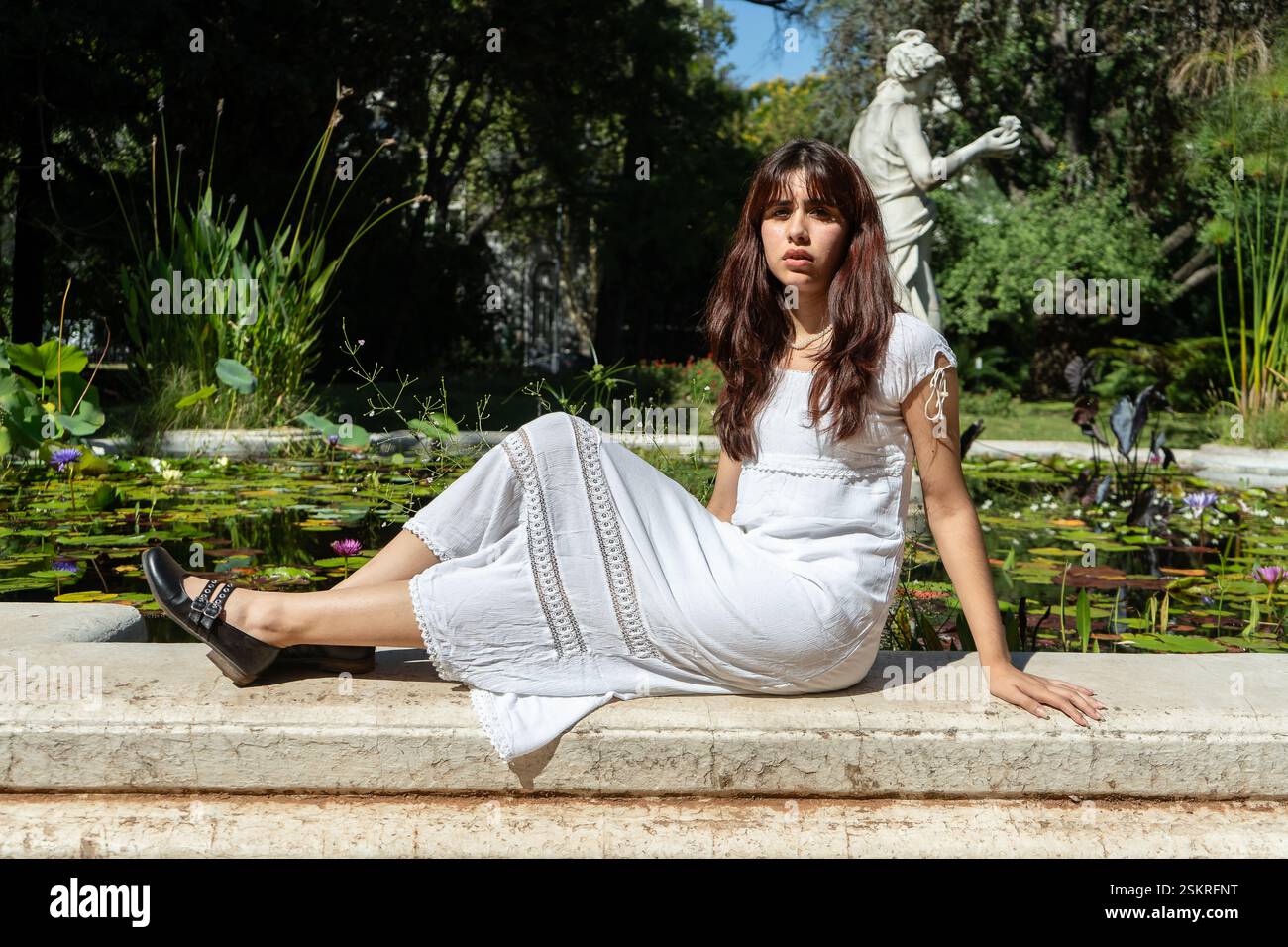 Fashion model posing by a pond in a botanical garden, wearing a white ...