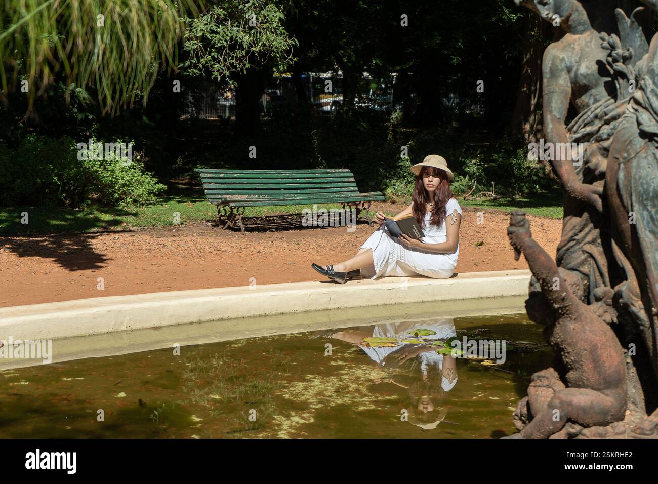 Tourist enjoying a relaxing moment reading a book by a pond in a ...