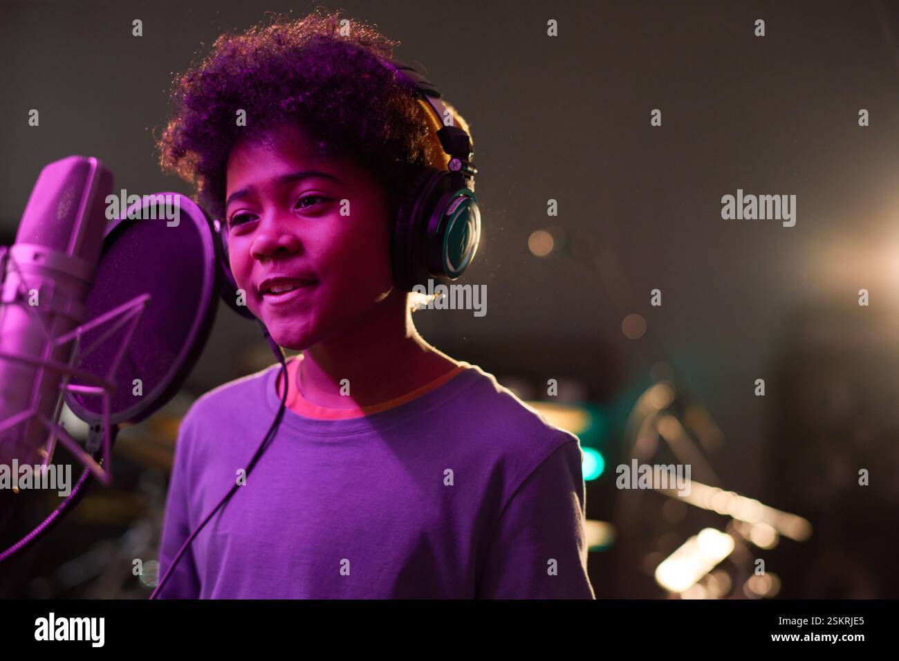 Wide shot of smiling teen boy wearing headphones while singing into microphone at professional ...