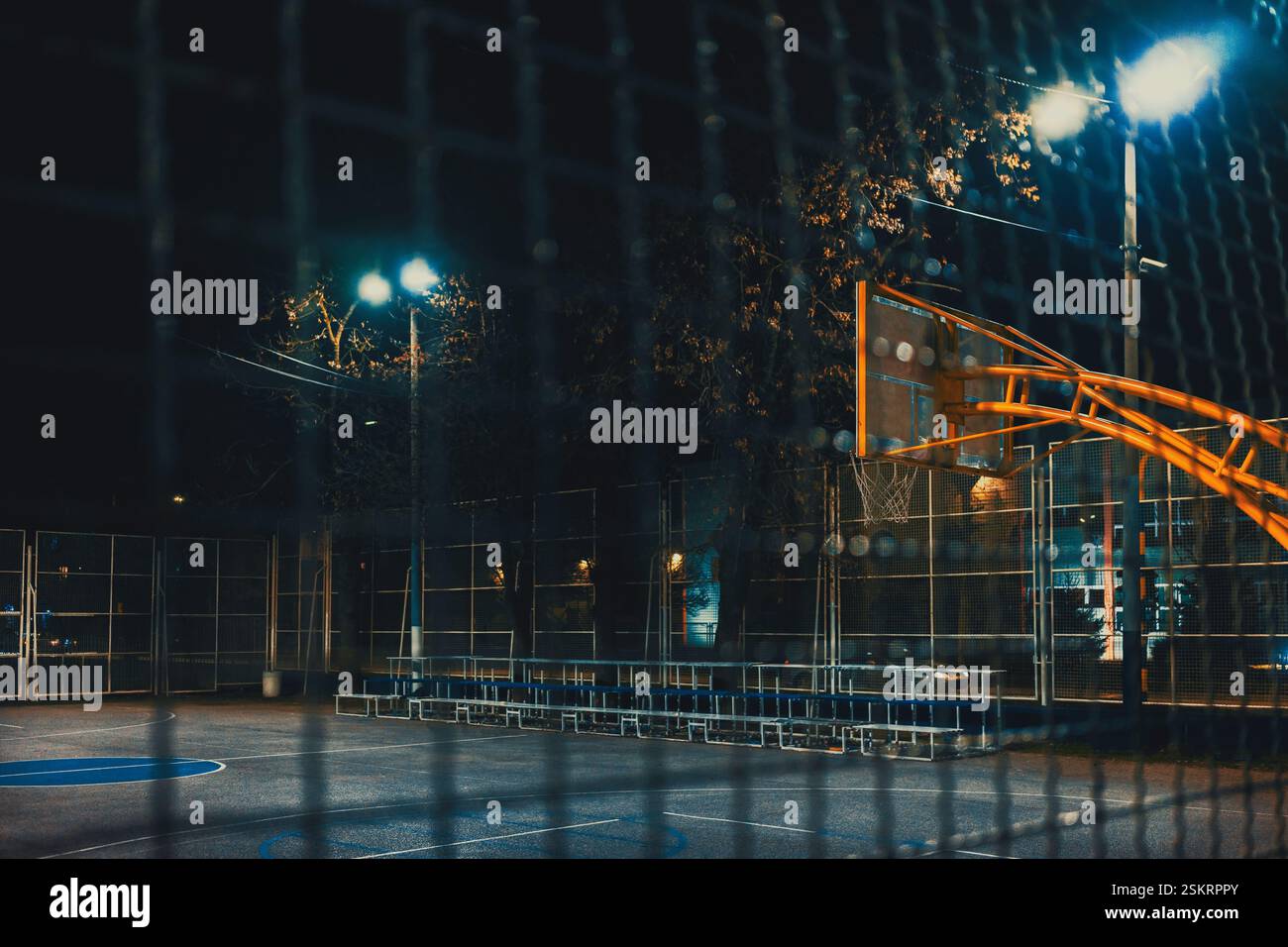 A view of the street basketball court at night, seen through the fence ...