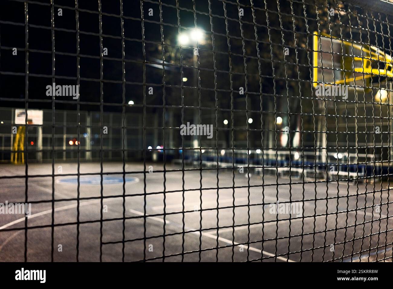 A view of the street basketball court at night, seen through the fence ...