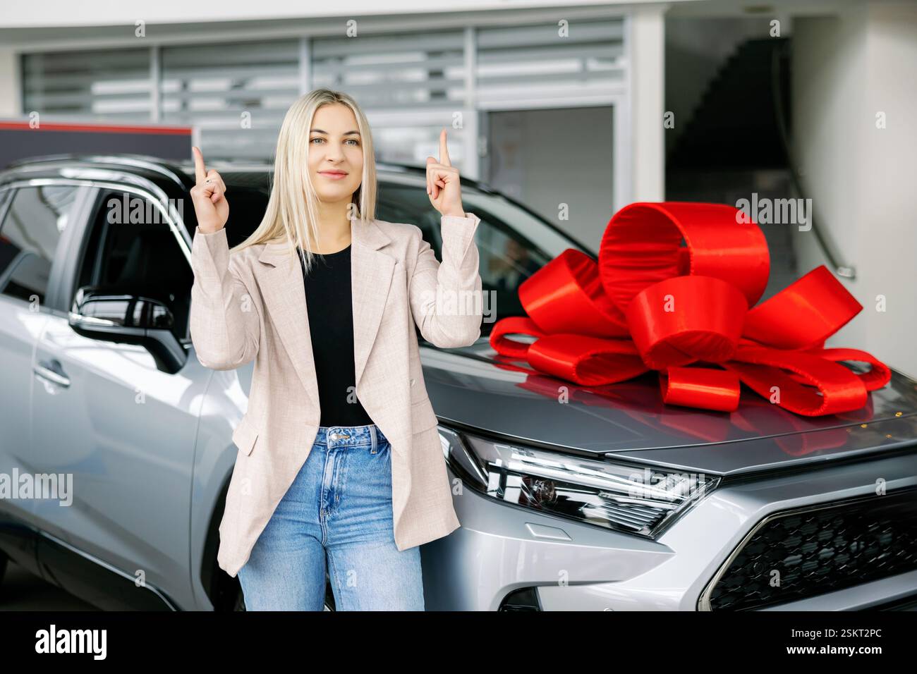 Saleswoman pointing upward while standing beside a new car adorned with ...