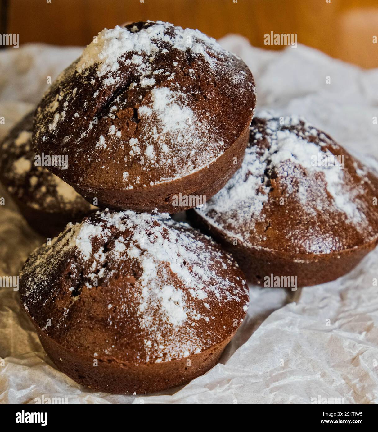 Stack of chocolate muffins dusted with powdered sugar on crinkled ...