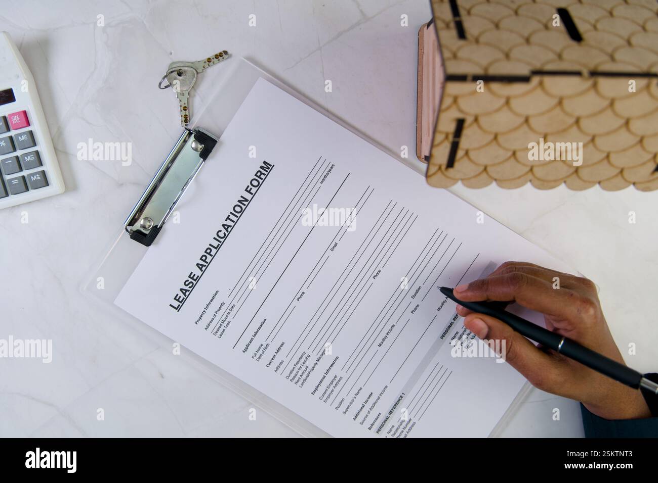 A person completes a lease application form on a desk with a calculator ...