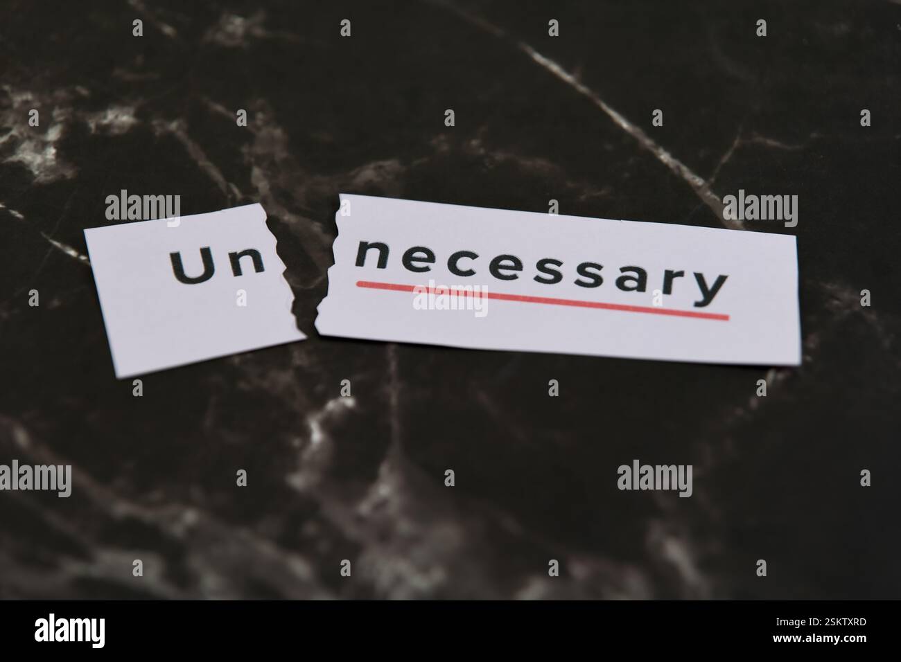Torn paper pieces display the word unnecessary on a dark marble surface ...