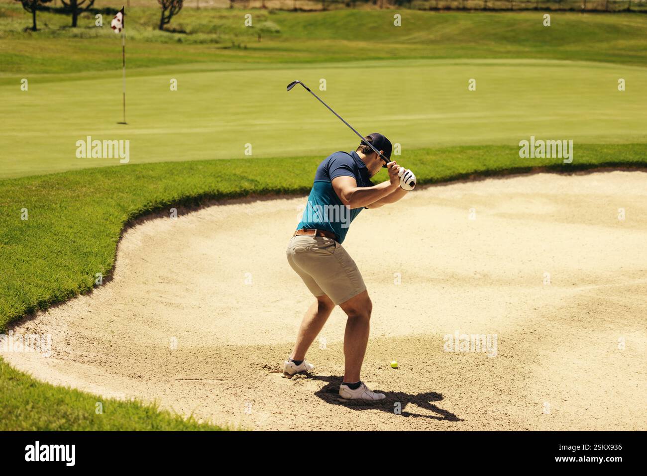 A determined sportsman swings a golf club in a sand bunker, aiming for ...