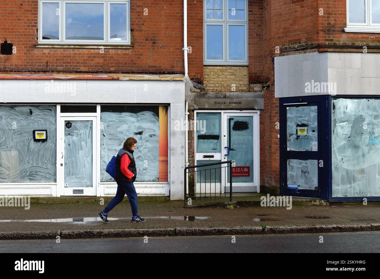 A woman pedestrian walking past closed down shopfronts in an urban town ...