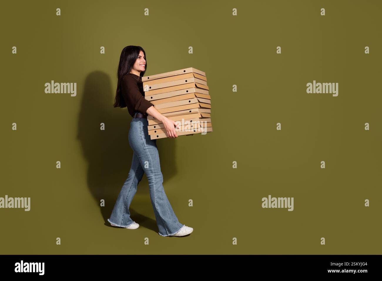Stylish young woman carrying stack of boxes against khaki background ...