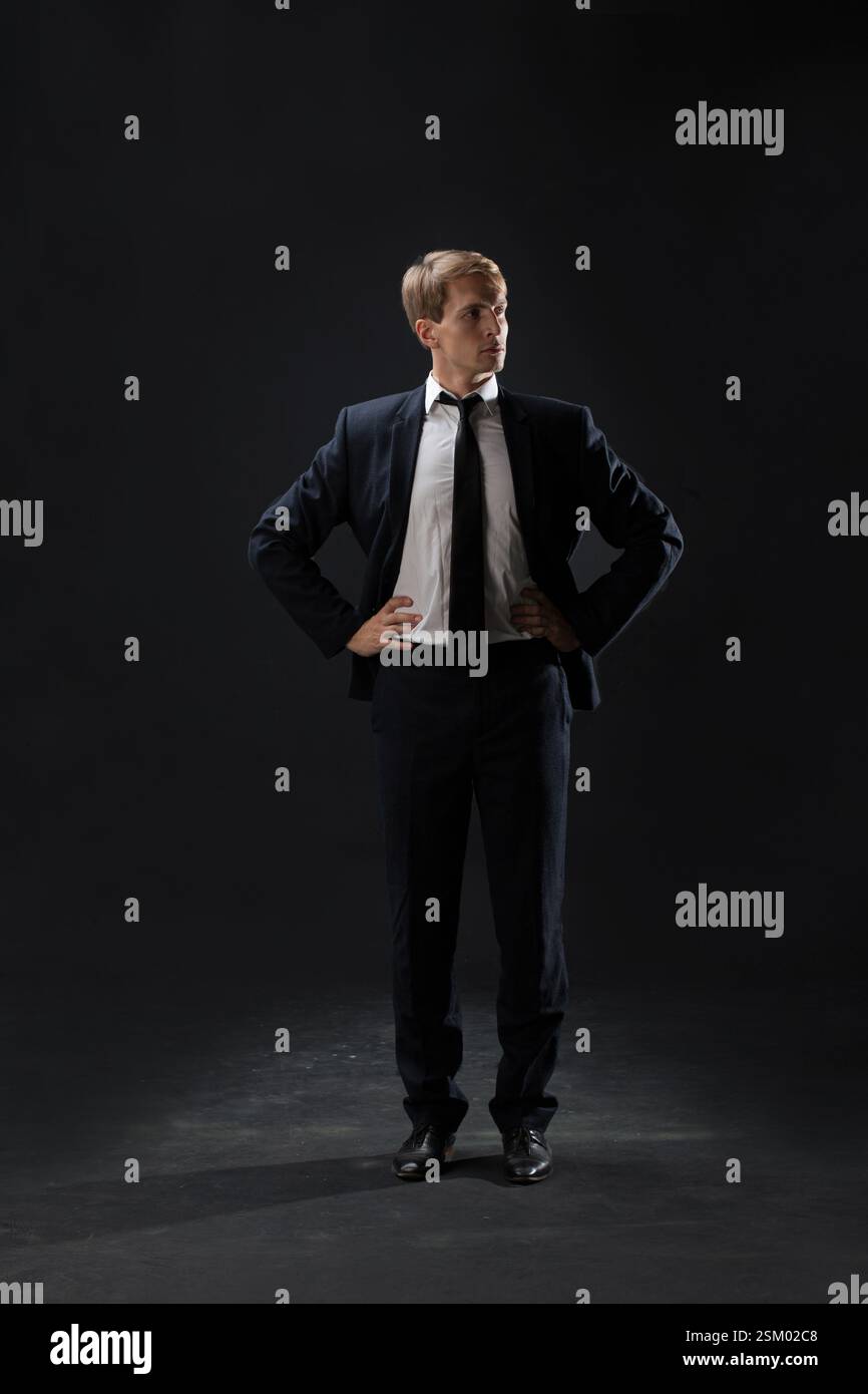 In a dark studio, a man stands confidently in a crisp black suit and ...