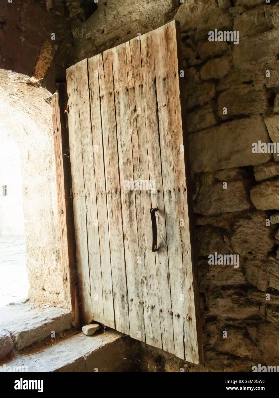 An aged wooden door stands ajar, revealing a stone passageway bathed in ...