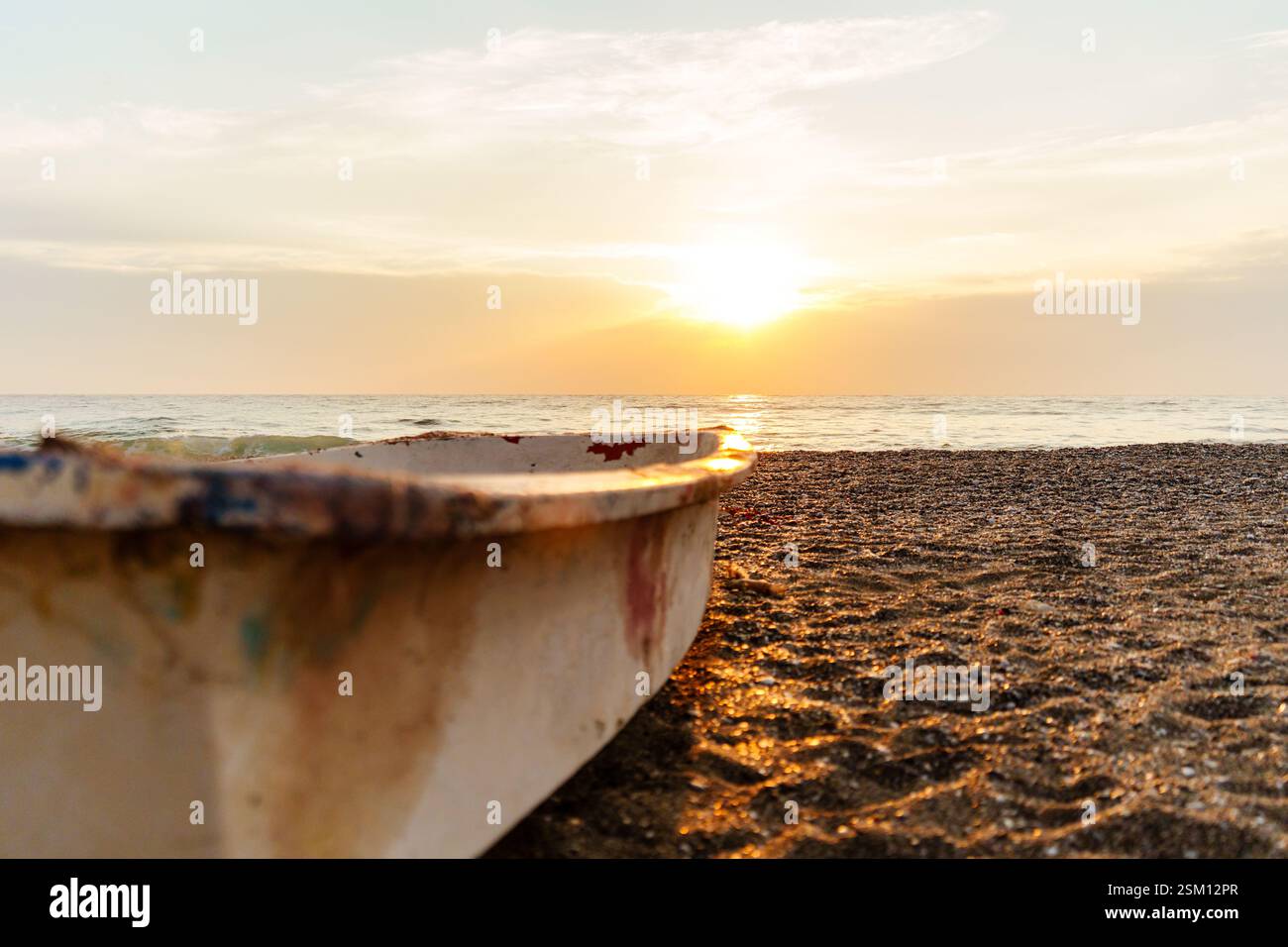 A tranquil sunset over a beach with an aging boat resting on the sand ...