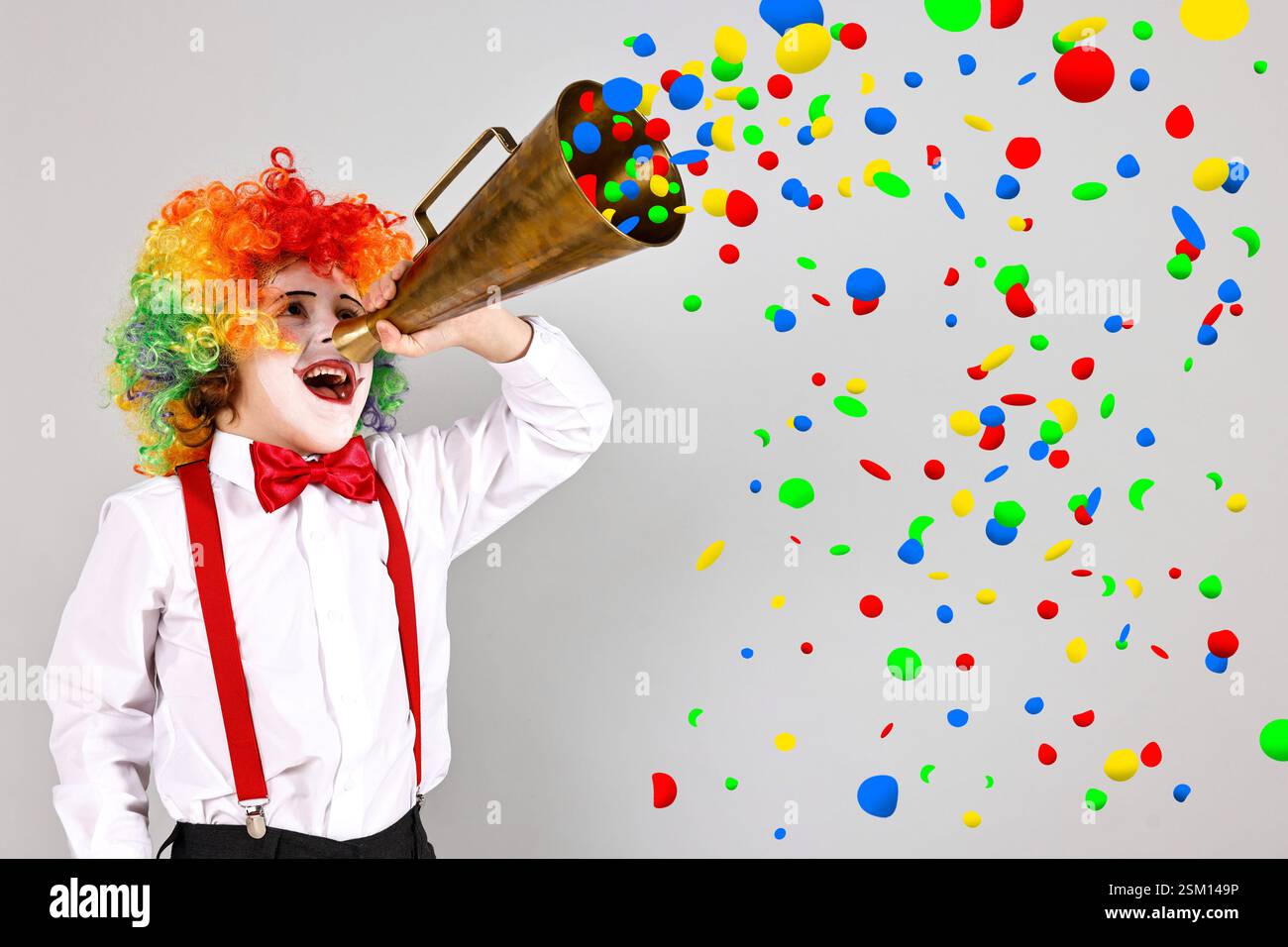 Cute boy dressed like clown shouting in megaphone with confetti flying ...