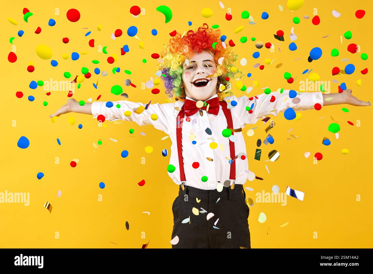 Happy boy dressed like clown under falling confetti on orange ...