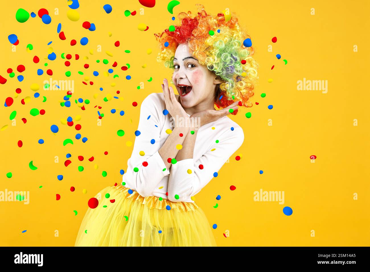 Happy girl dressed like clown under falling confetti on orange ...
