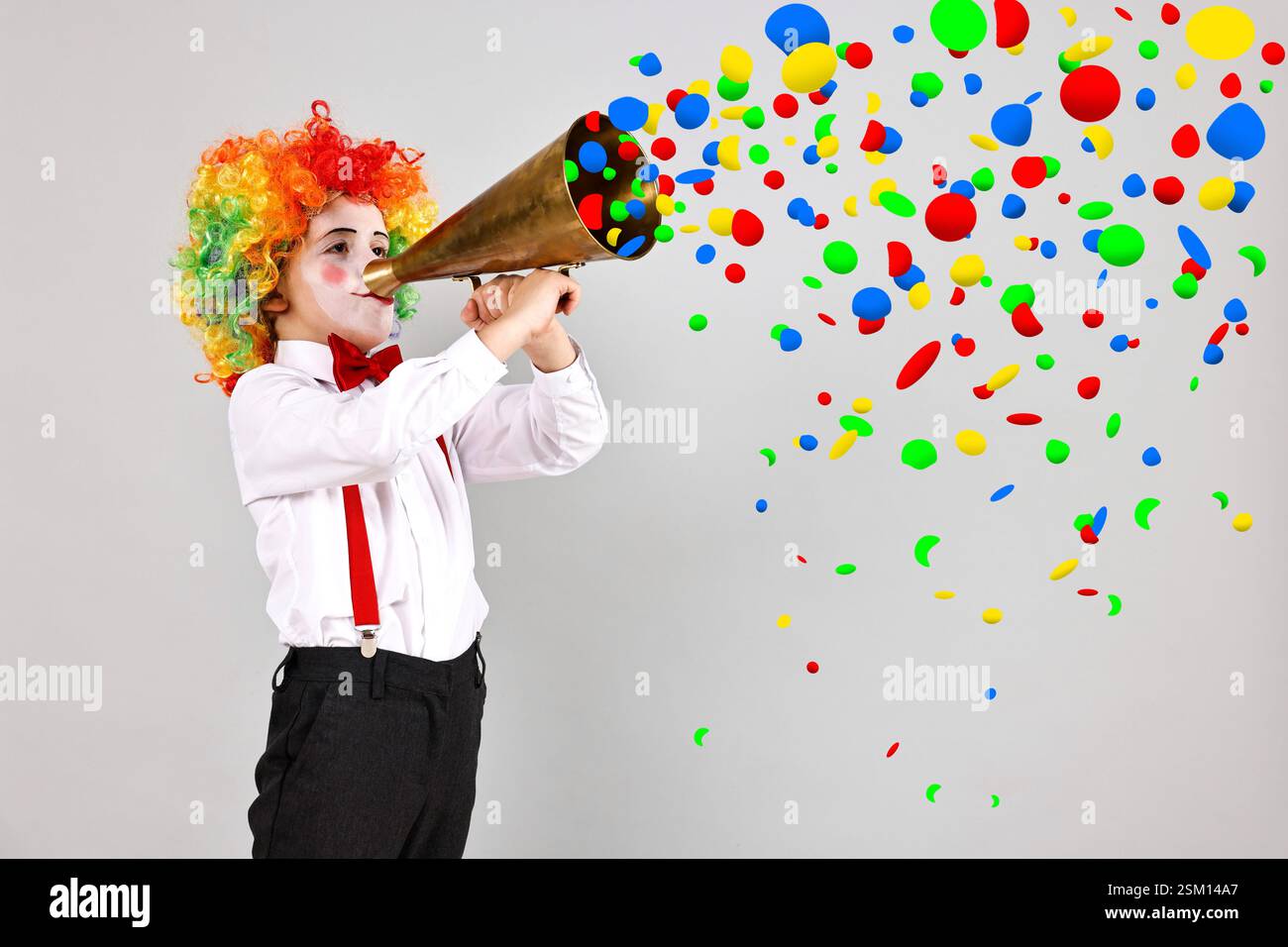 Cute boy dressed like clown shouting in megaphone with confetti flying ...