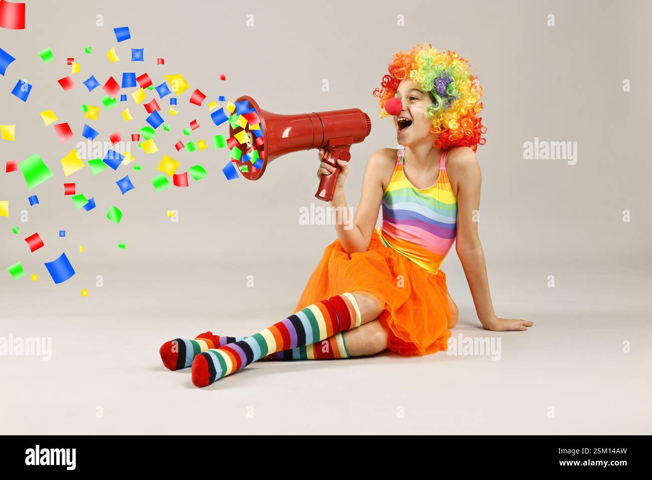 Cute girl dressed like clown shouting in megaphone with confetti flying ...