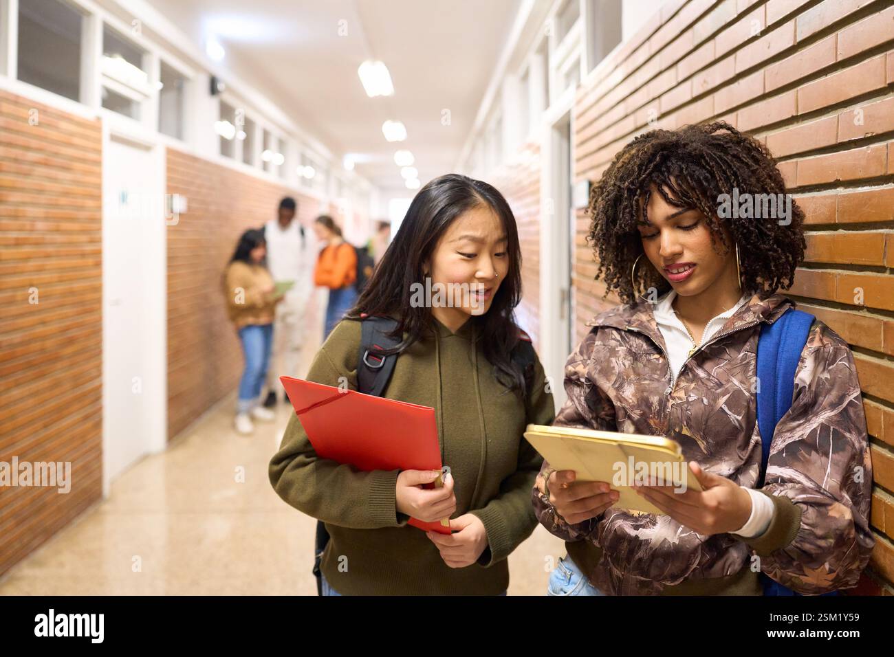 Two students sharing notes walking down school hallway Stock Photo - Alamy
