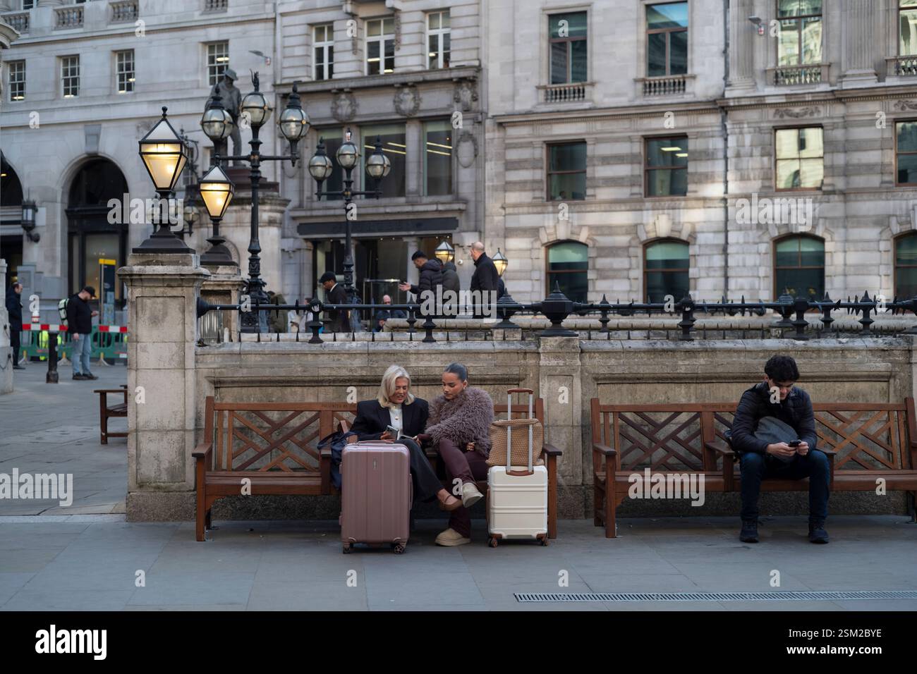 Women with suitcases sit on benches along Cornihill, historic financial ...