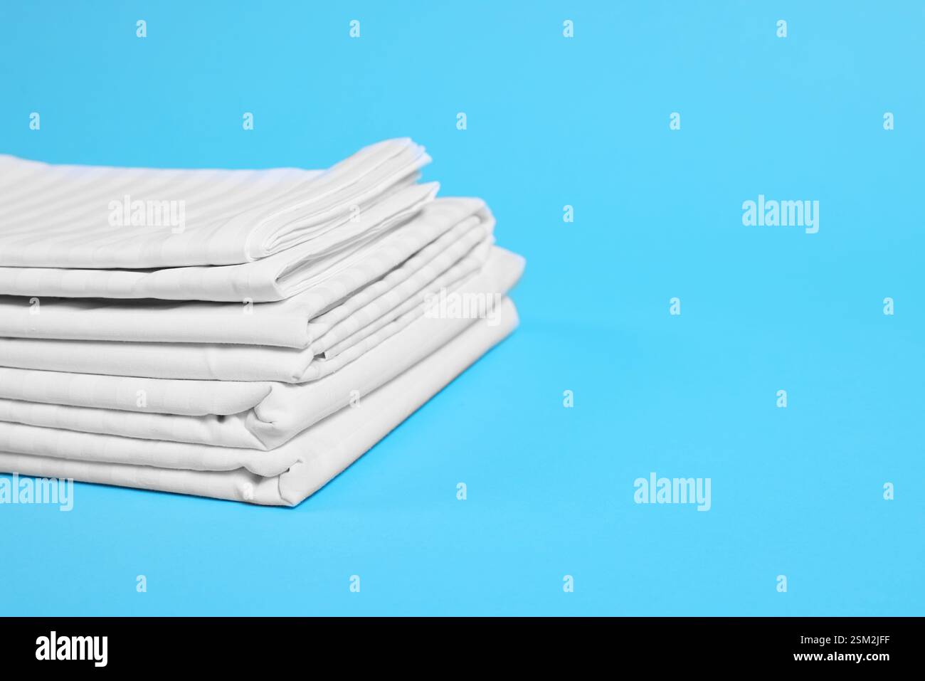 Stack of clean bed linens on light blue background, closeup. Space for ...