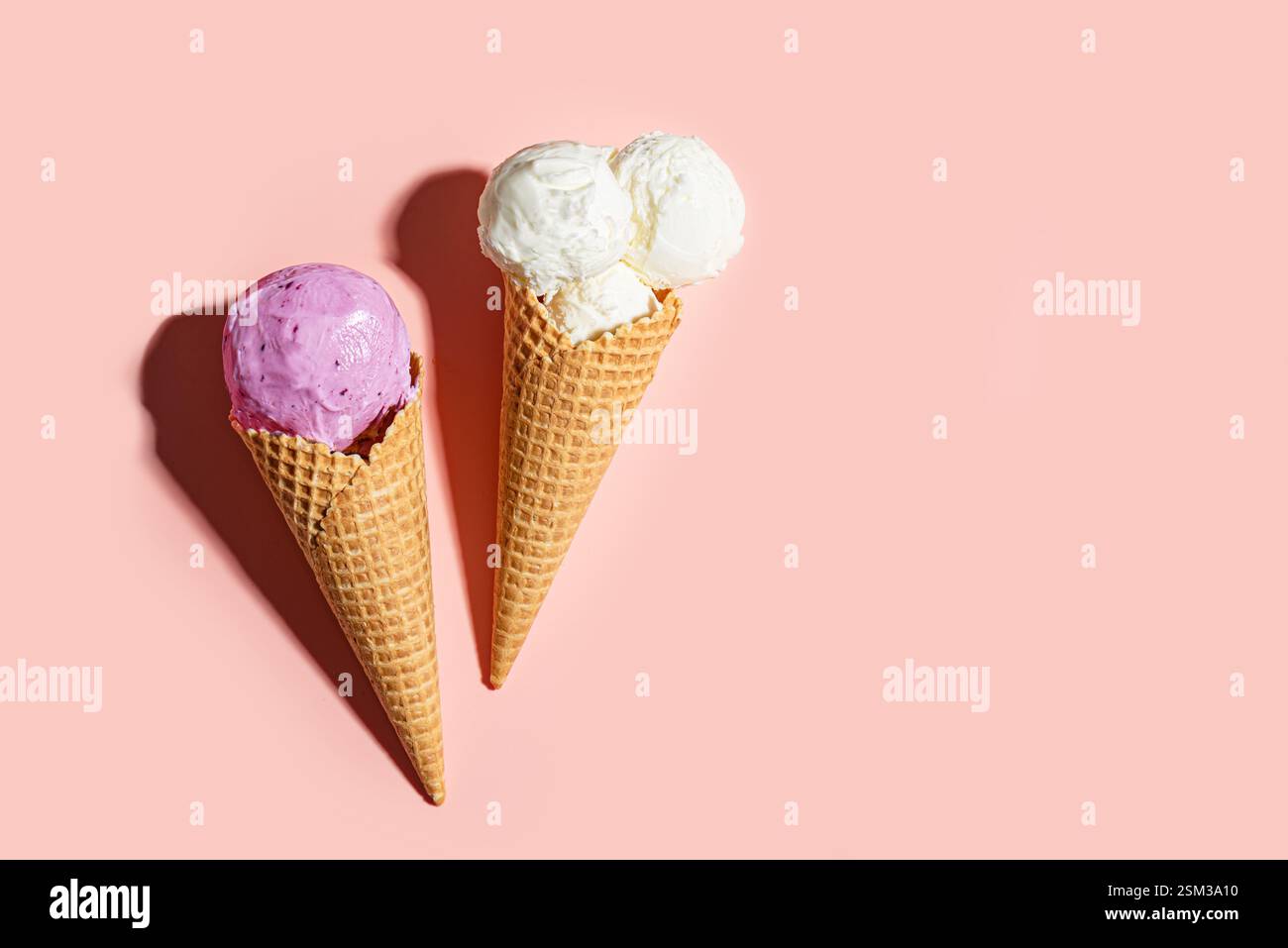 Two crispy ice cream cones vanilla and blueberry flavors on pink pastel ...