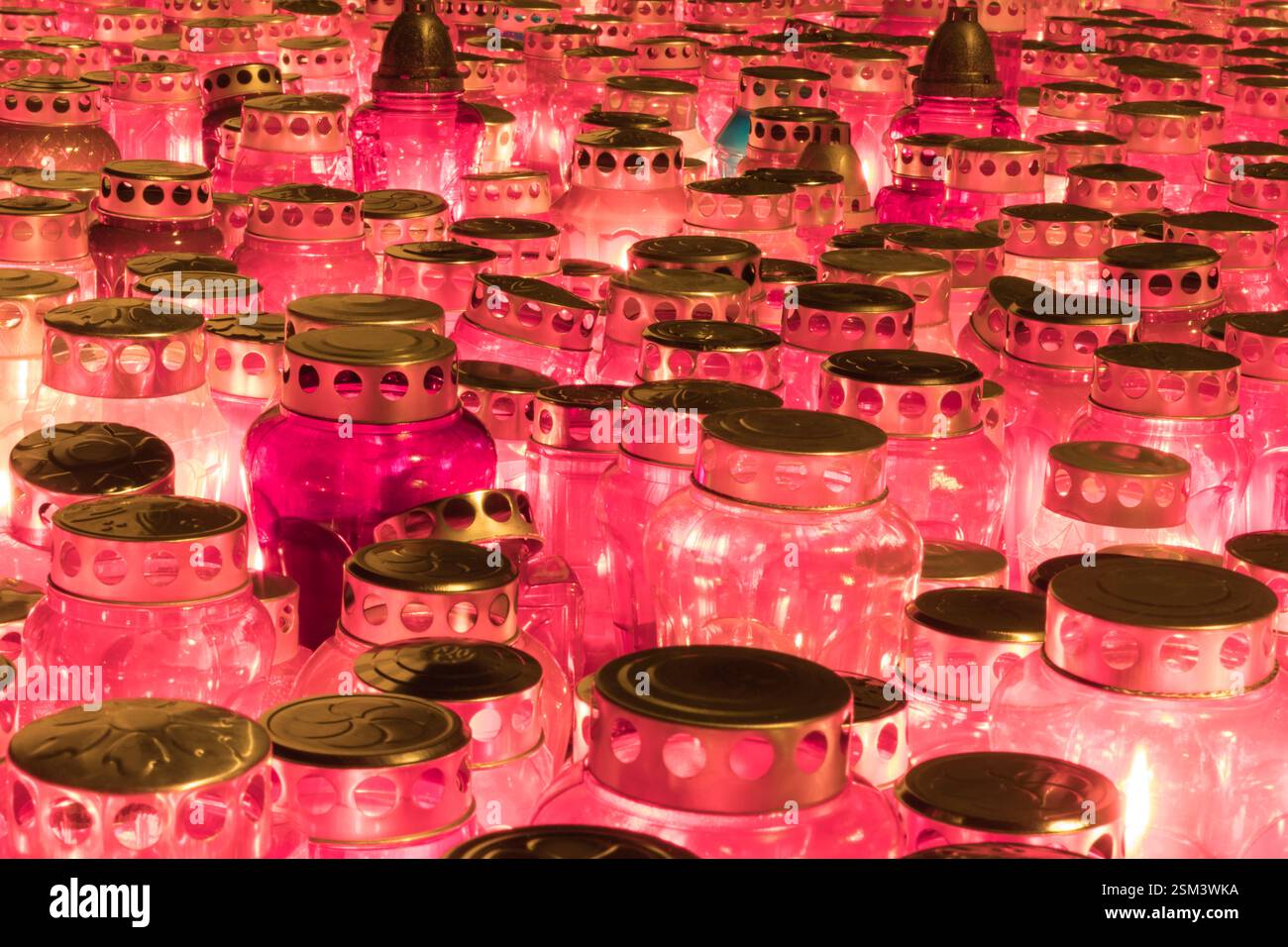 Brightly glowing red memorial candles with intricate metallic covers ...