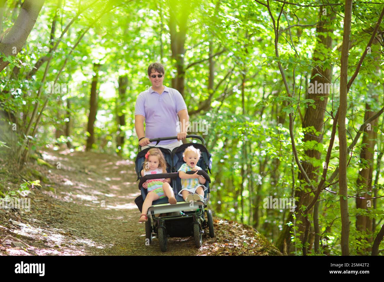 Young father walking in a park with children in stroller. Dad and kids ...