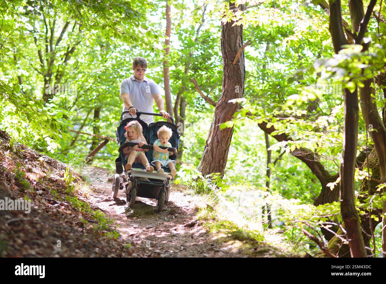 Young father walking in a park with children in stroller. Dad and kids ...