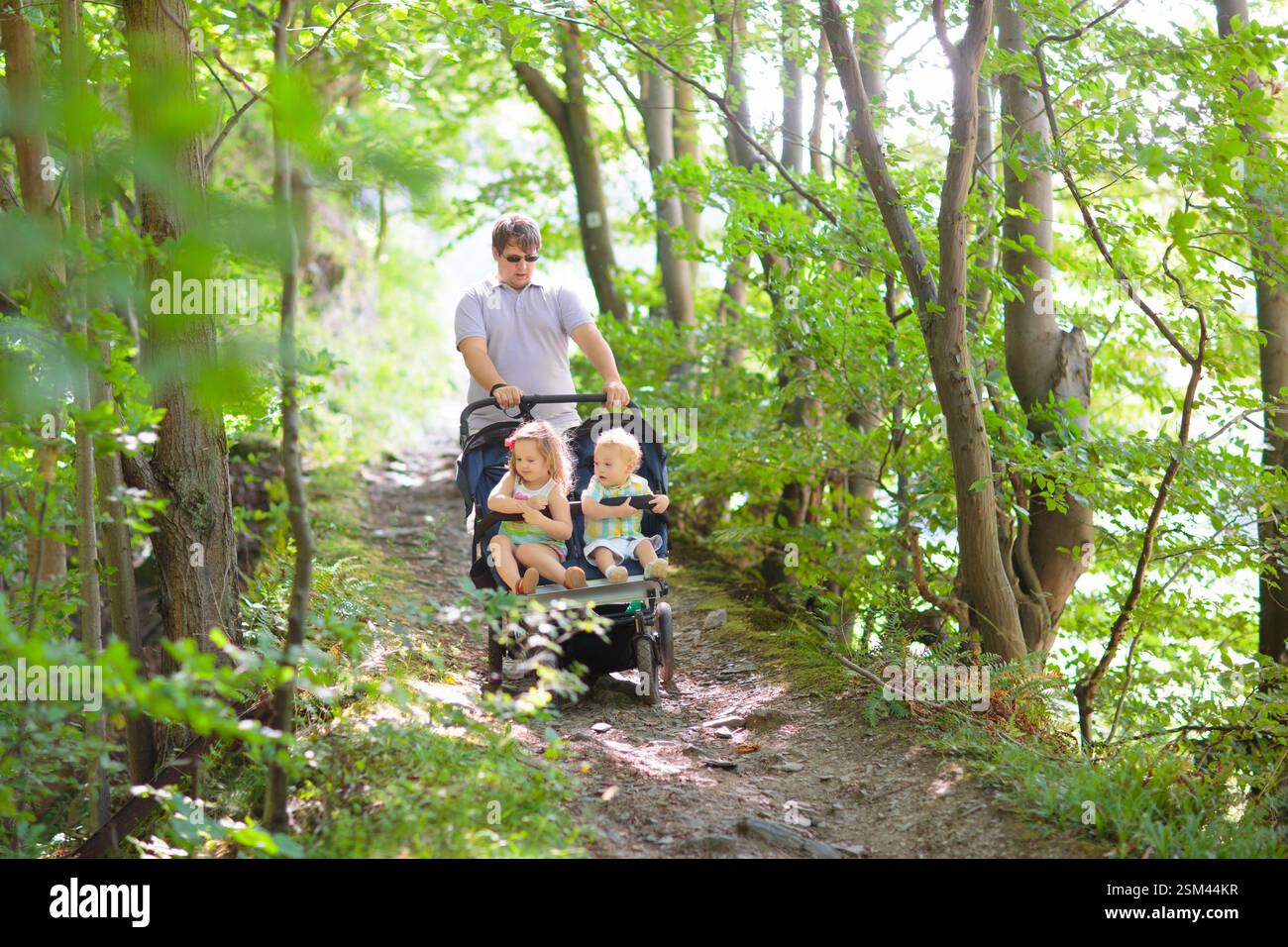 Young father walking in a park with children in stroller. Dad and kids ...