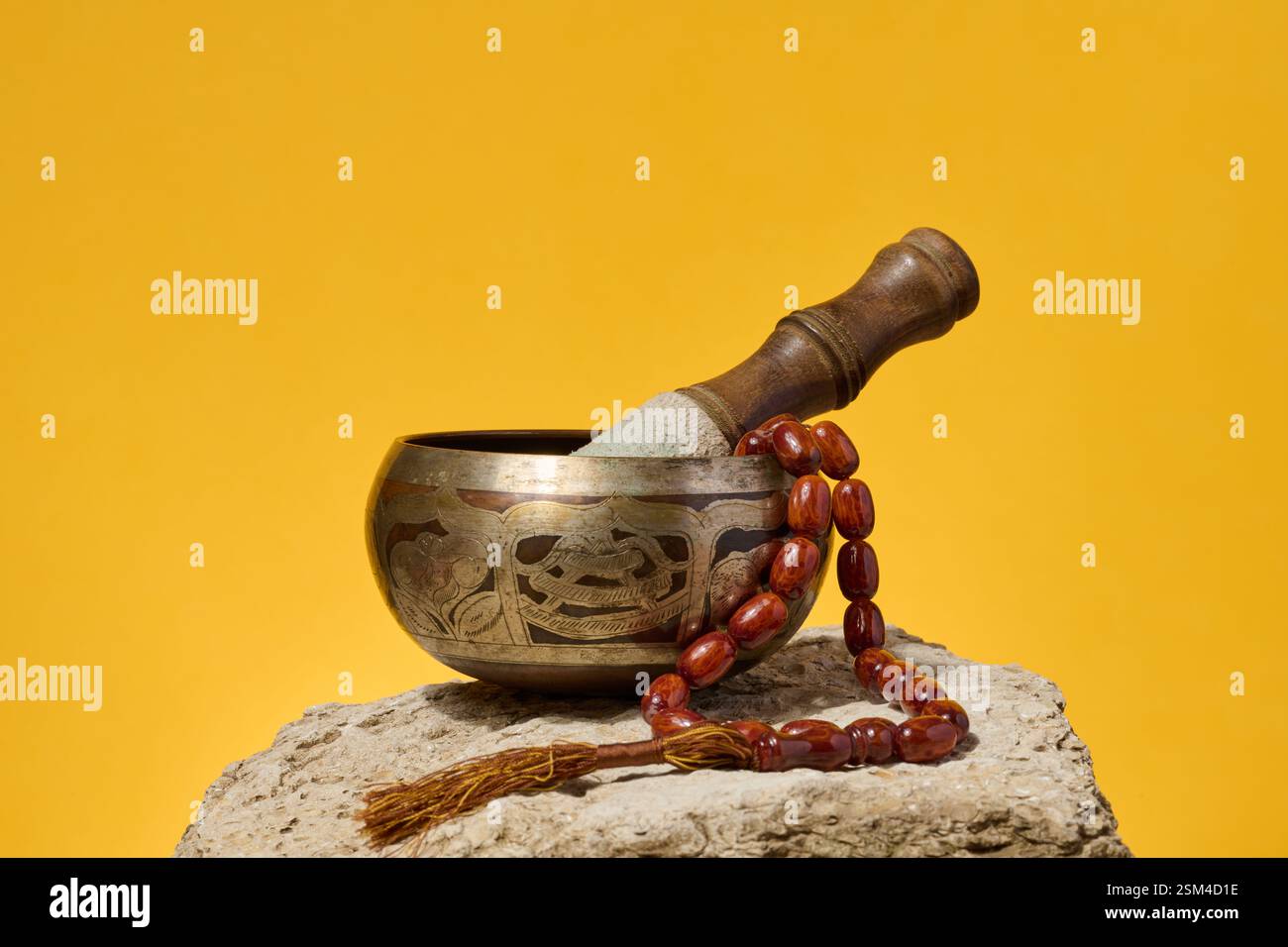 Copper singing bowl, wooden stick and prayer beads on stone, yellow ...