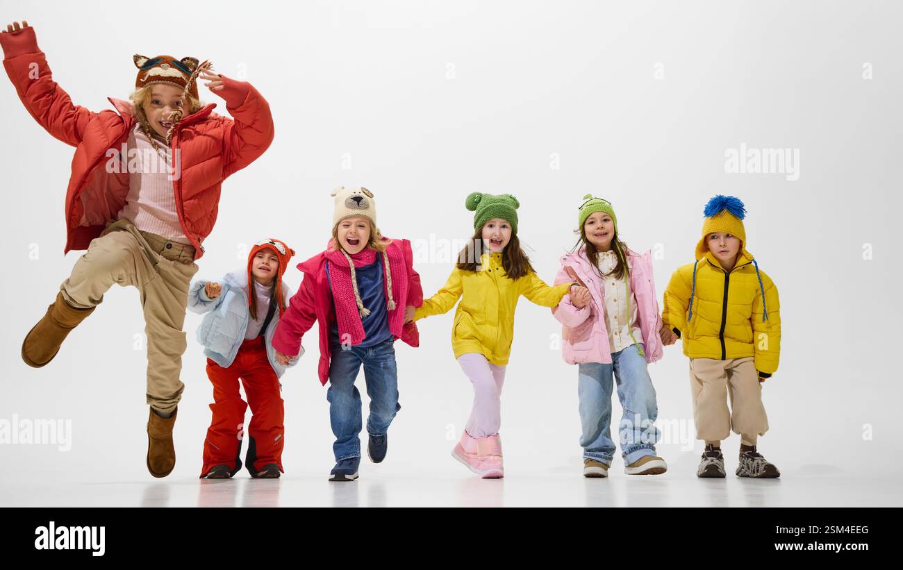 Group of children, holding hands, mid-jump, wearing cozy winter clothes ...