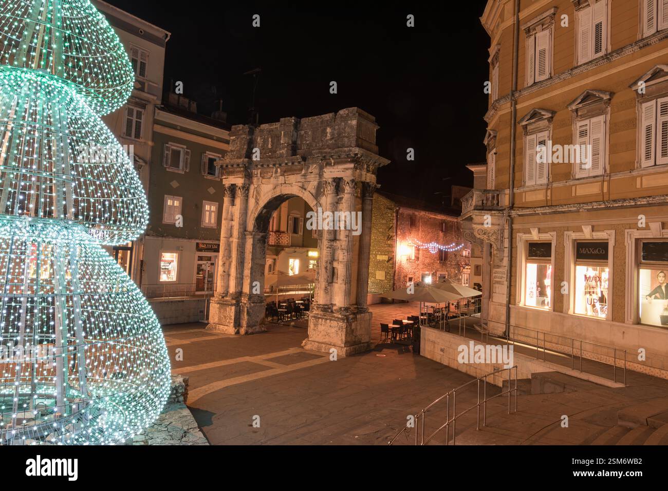 An ancient stone arch and nearby structures brightly light up with ...