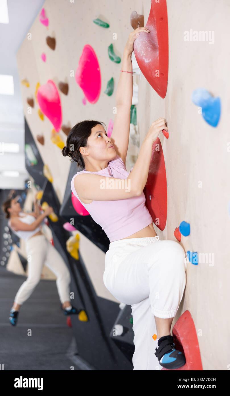 Sporty woman climbing on bouldering wall demonstrating physical strength, technical skill, and ...