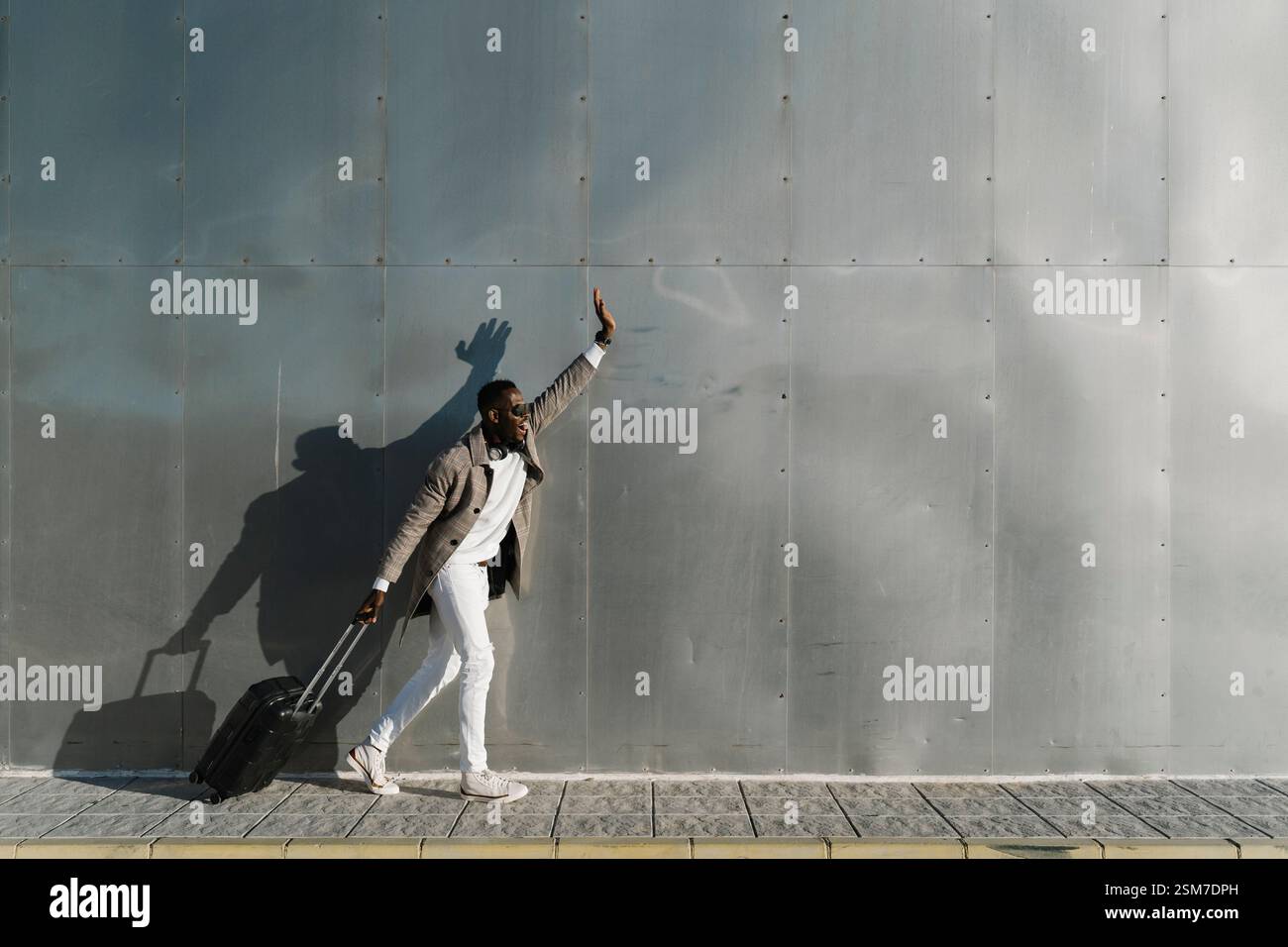 Stylish black man waving goodbye while walking with luggage Stock Photo ...