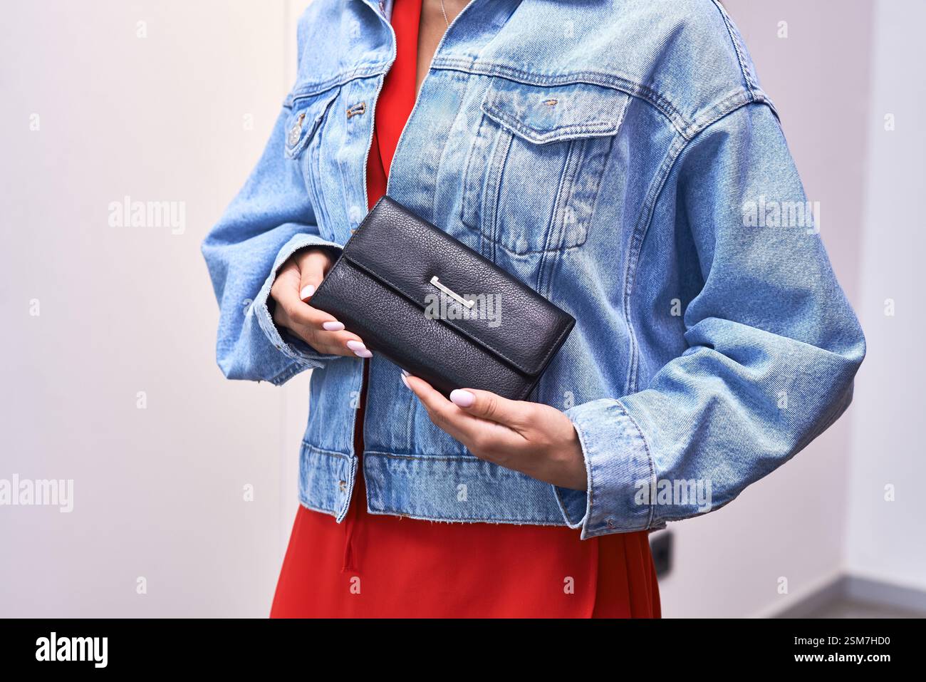 Stylish black wallet held by woman in denim jacket and red dress ...
