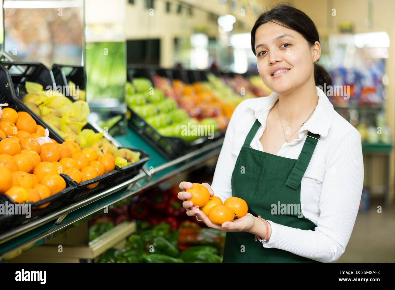 Female grocery store worker lays out ripe tangerines on counter and ...