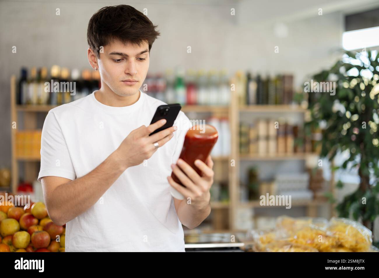 In shop young man scans QR code and take reading on ketchup package using phone camera Stock ...