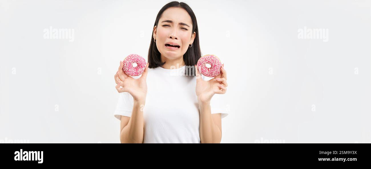 Crying asian woman showing tasty douhnuts and sobbing, being on healthy ...