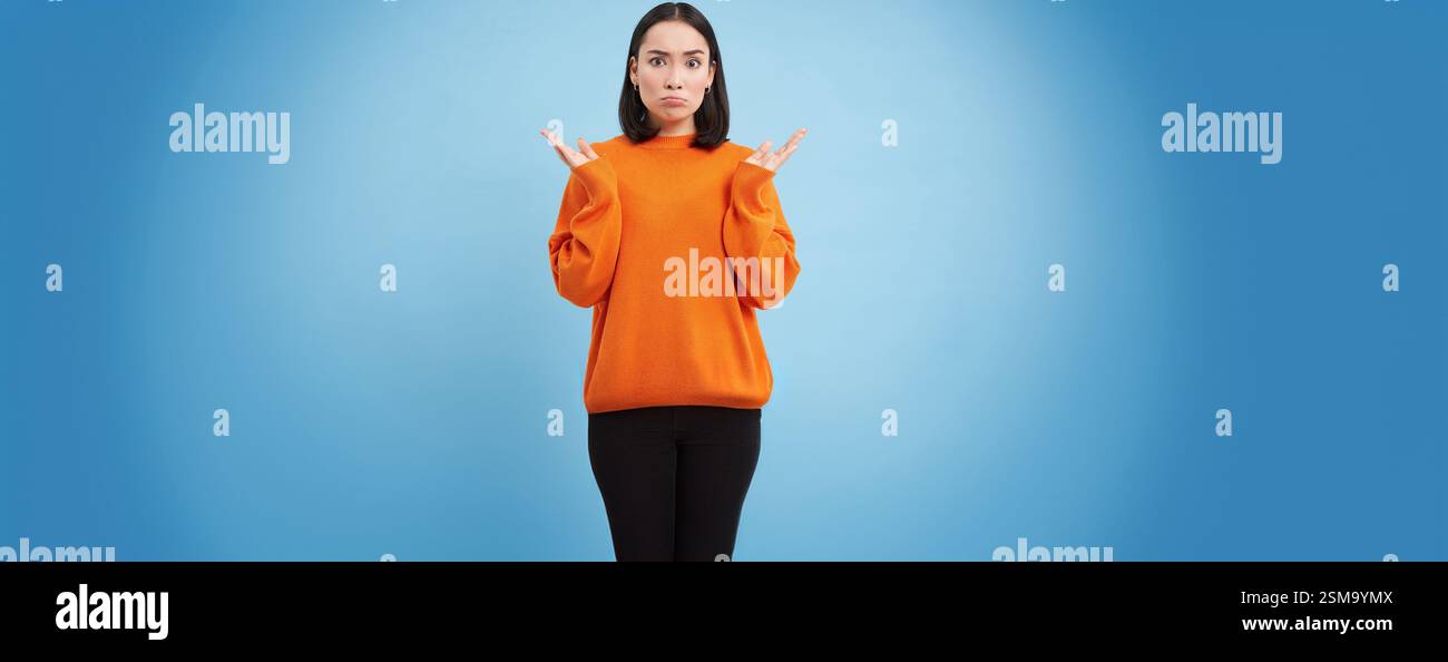 Asian girl with confused face, shrugs shoulders and pouts, looks upset ...
