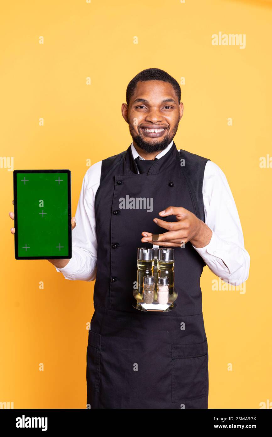 Smiling waiter in uniform presenting a device with isolated chroma key ...