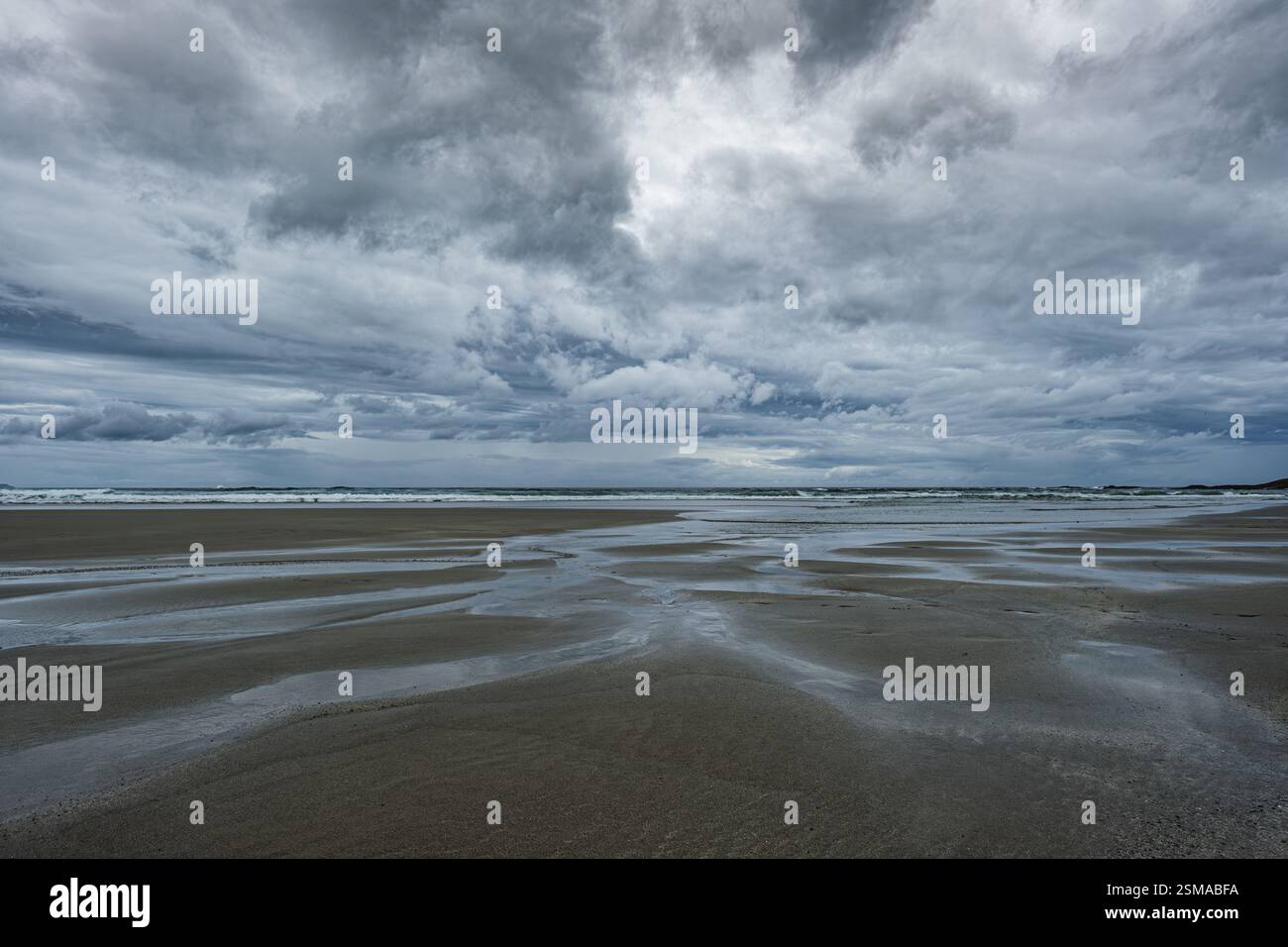 The receding tide reveals intricate patterns in the wet sand, under a ...