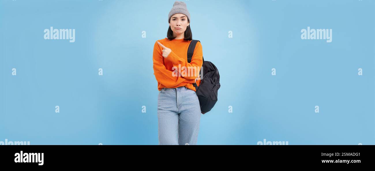 Skeptical asian woman pointing left at strange banner, looks doubtful ...