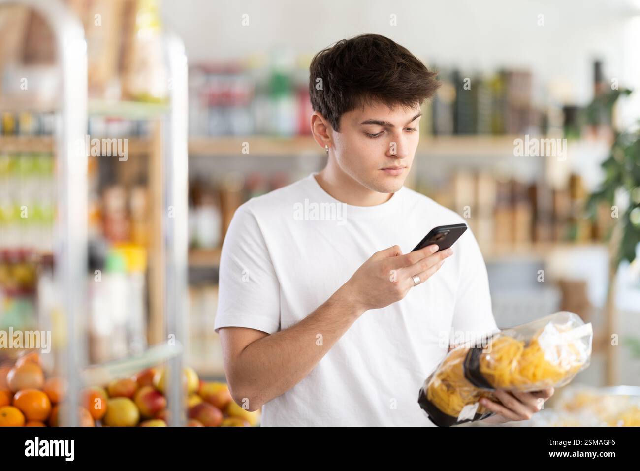 Guy using smartphone to scan barcode on pasta package in supermarket ...