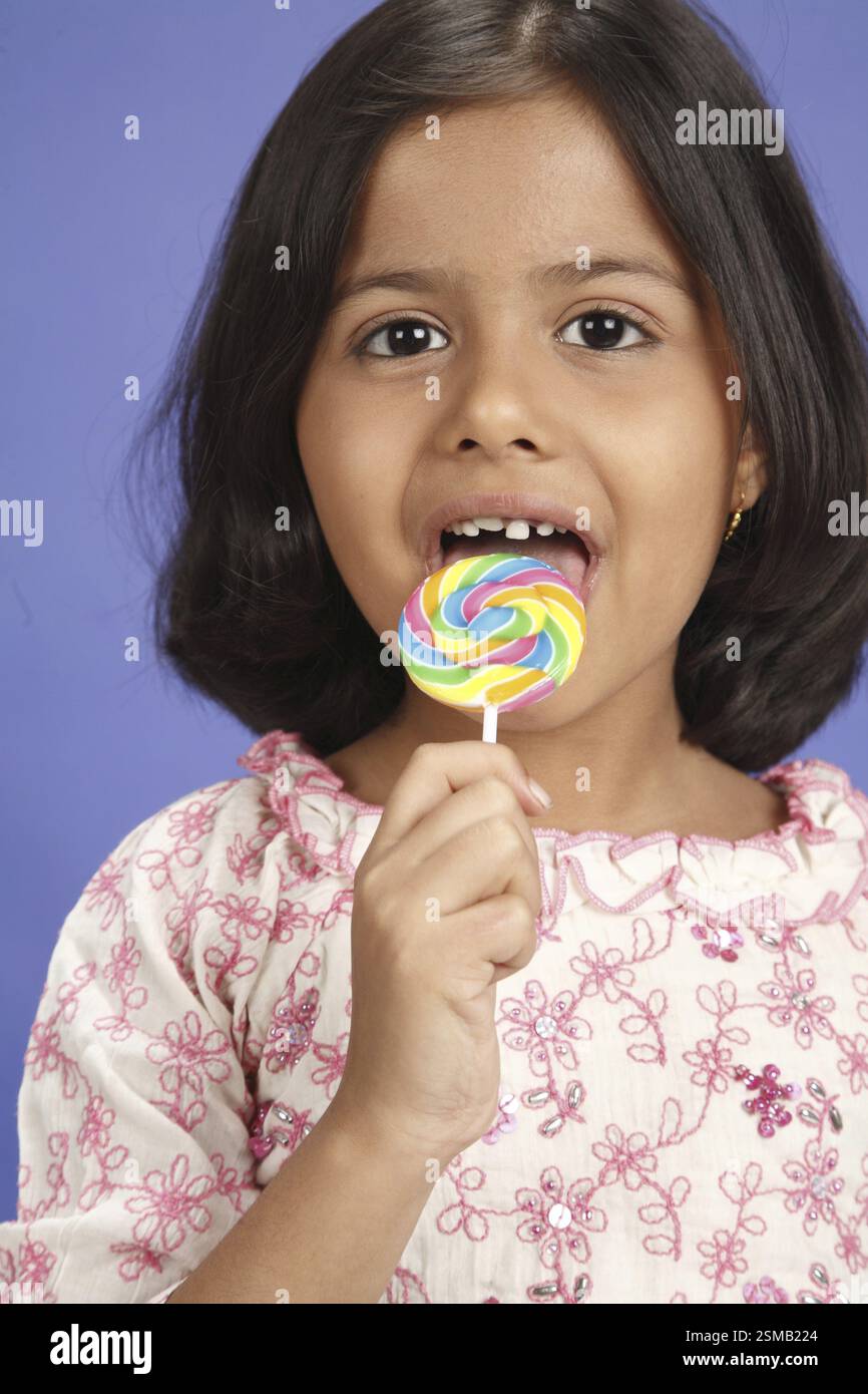 Eight year old girl holding large colourful lollipop licking it with tongue MR#703U Stock Photo ...