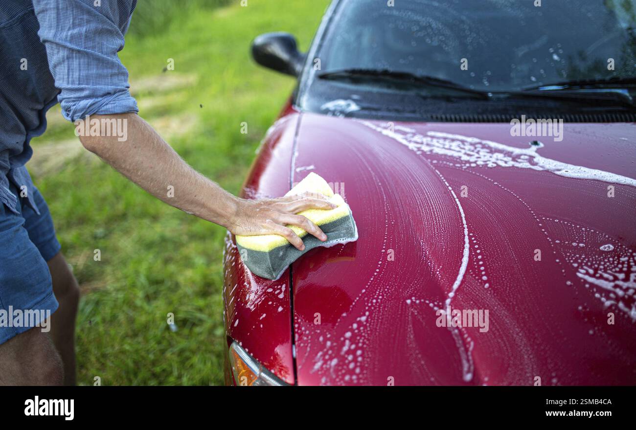 A red car being washed with a sponge and soap, surrounded by grass ...