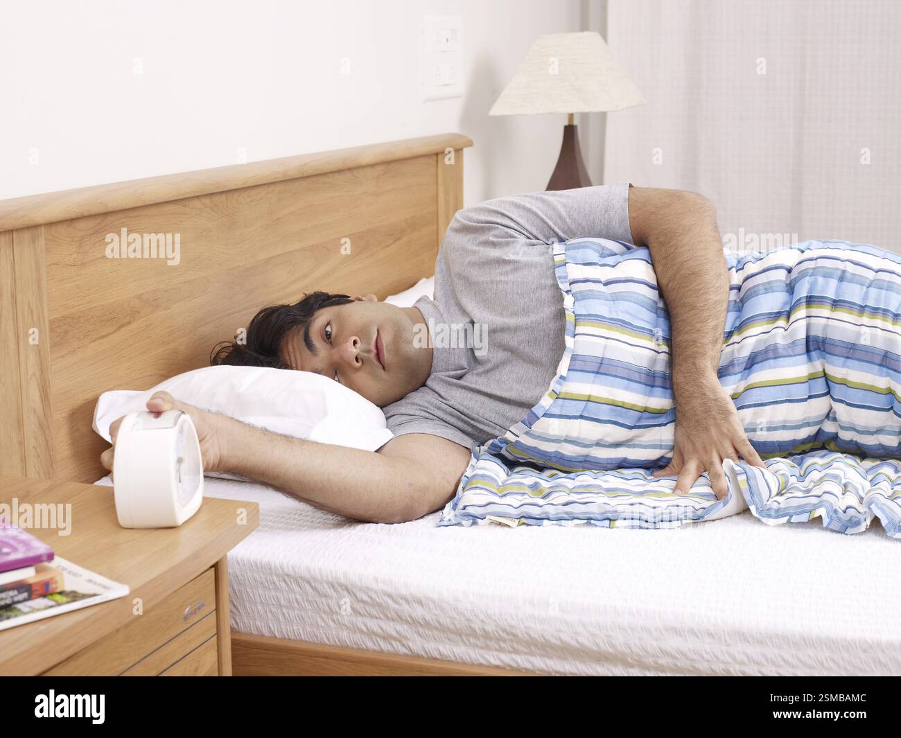 Young man laying on bed hand stopping ringing alarm clock MR#702V Stock ...