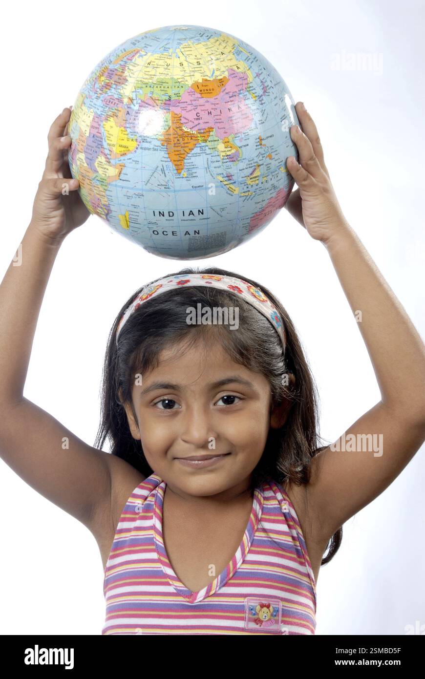 South Asian Indian six year old girl holding globe on head looking at ...